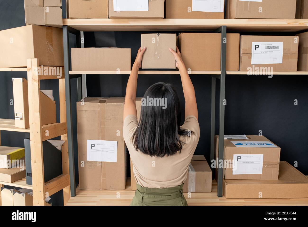 Back view of young brunette female manager taking one of packed boxes ...