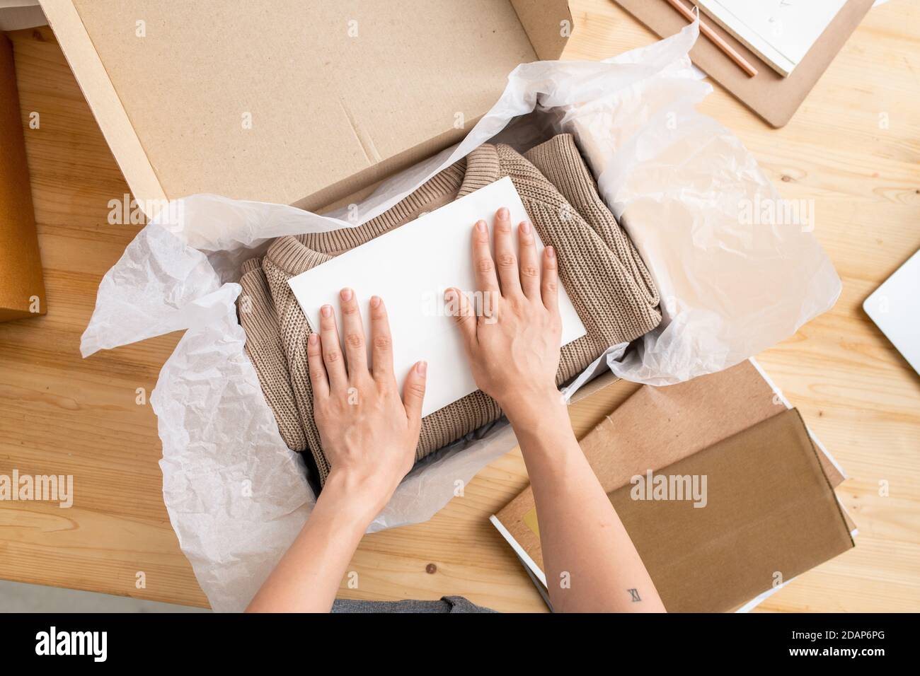 Hands of young manager of online shop putting paper on top of folded ...