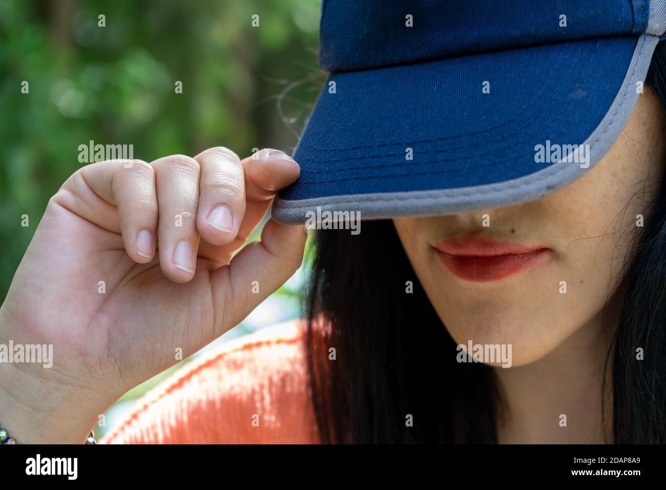 Woman hiding her face behind a blue basecap Stock Photo - Alamy