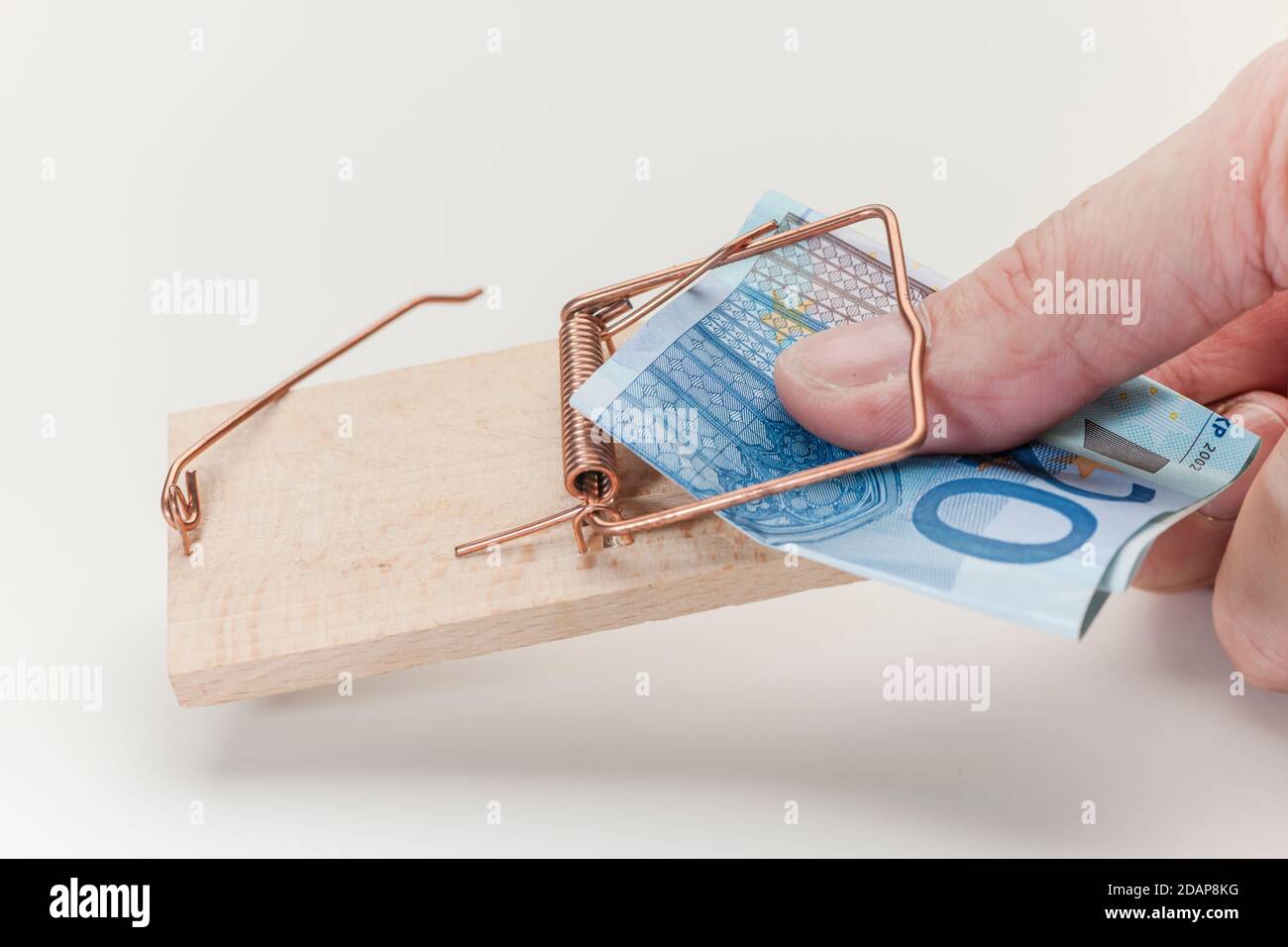 Thumb caught in a mousetrap when reaching for a 20 euro note on a white ...
