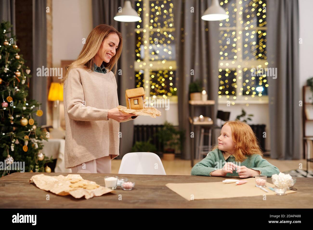 Happy young mother in casualwear carrying homemade gingerbread house ...