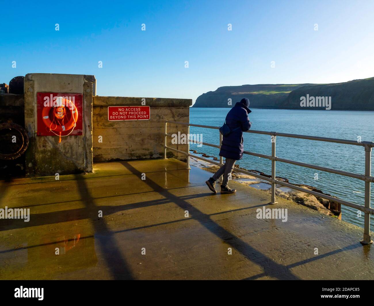 A senior lady leans on the handrail at the end of the harbour wall at ...