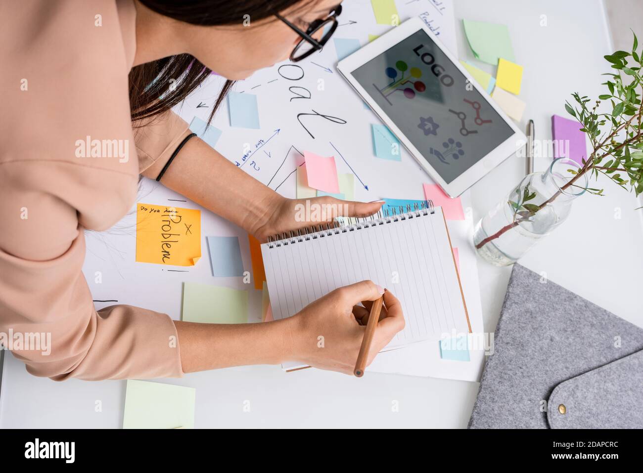 Young female designer making notes in copybook while bending over ...