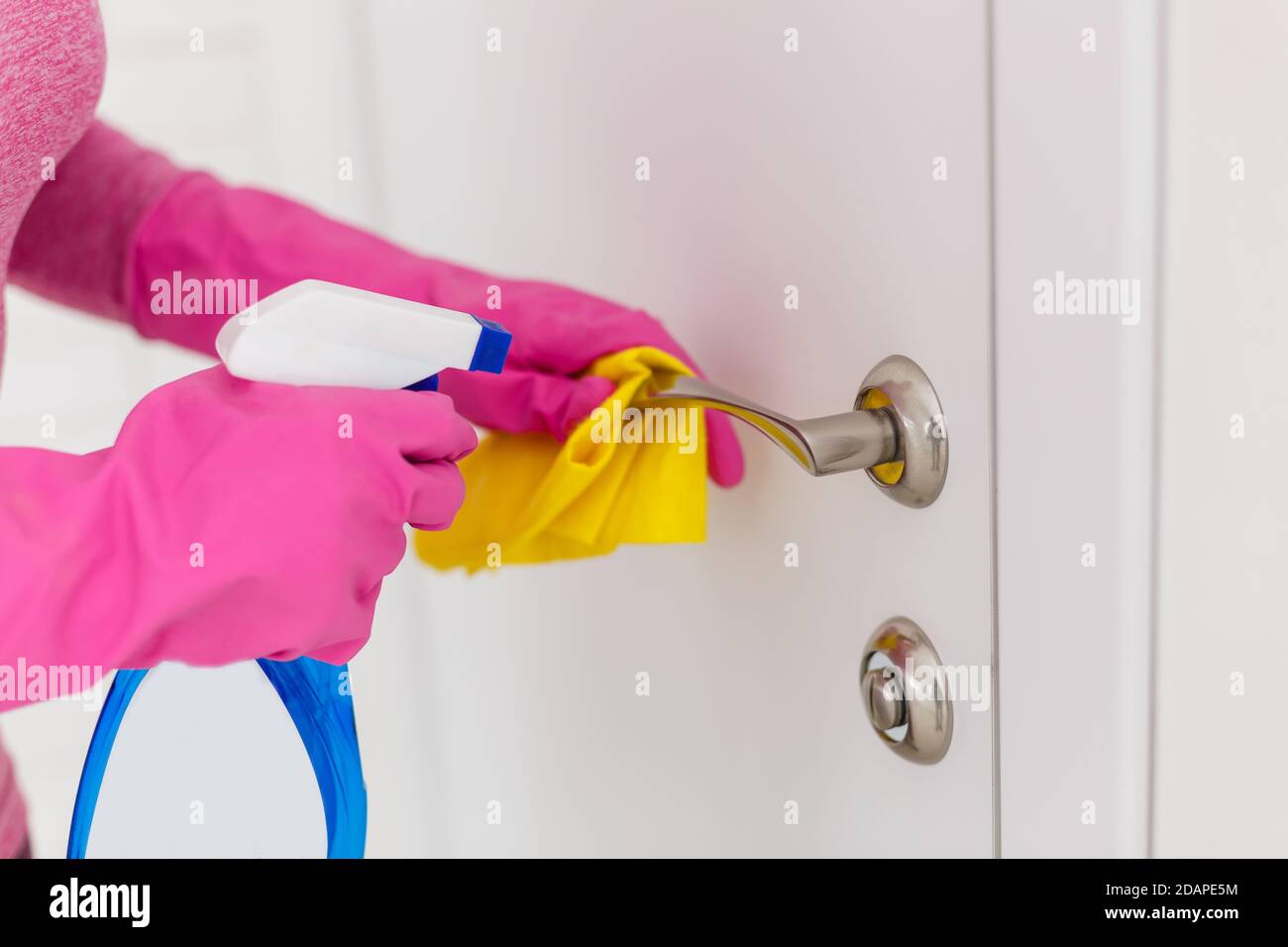 Woman cleaning a door handle with a disinfection spray and disposable ...