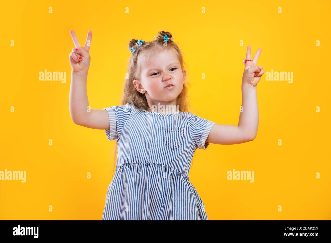 Funny little girl showing peace gesture on yellow background Stock ...