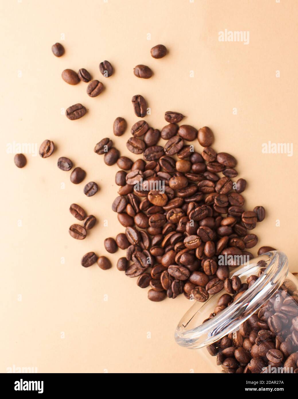 Closeup of coffee beans spill out of a glass jar on a light brown ...