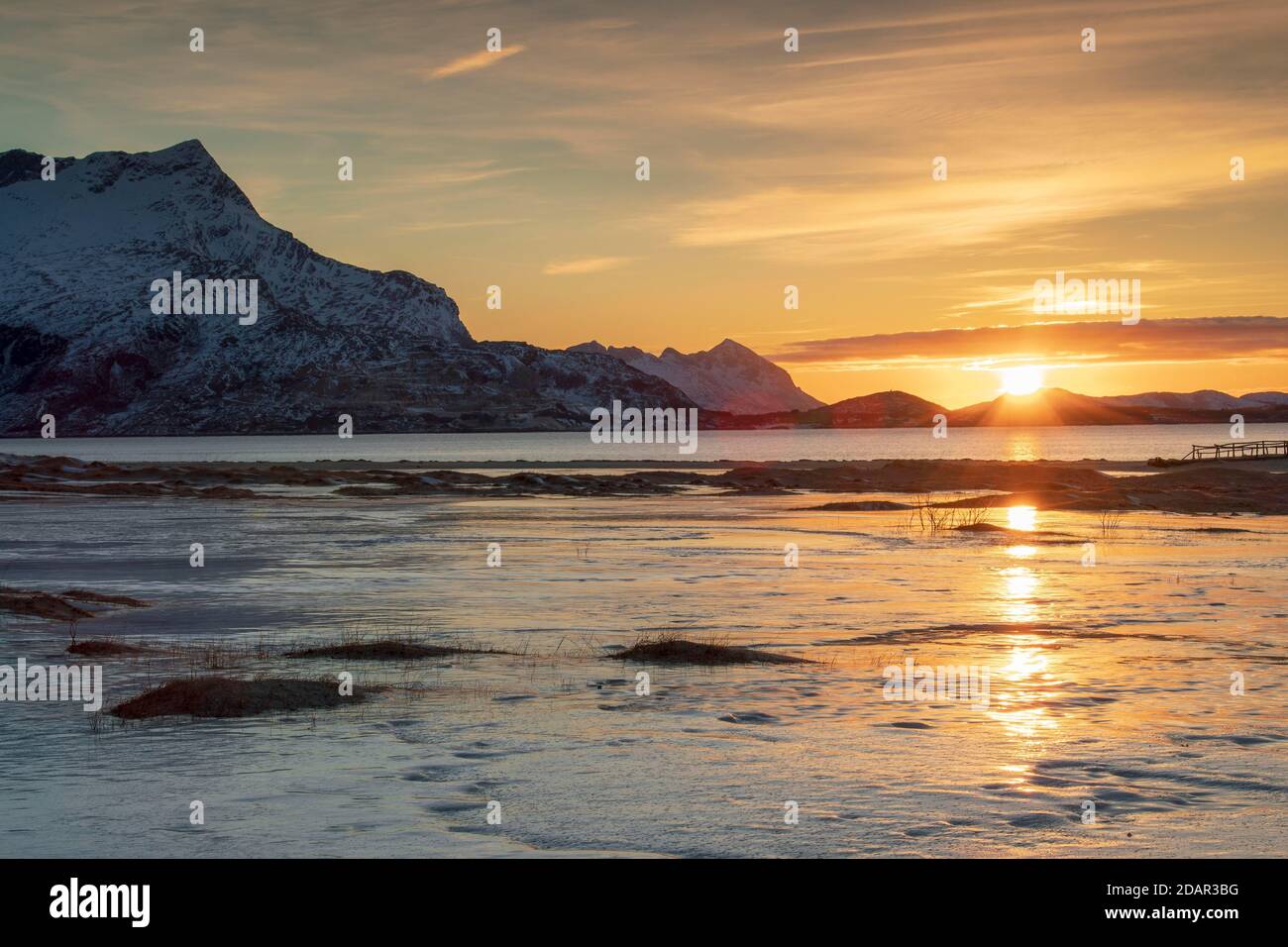 Sunset at sandy beach covered with ice, mountains in the back ...