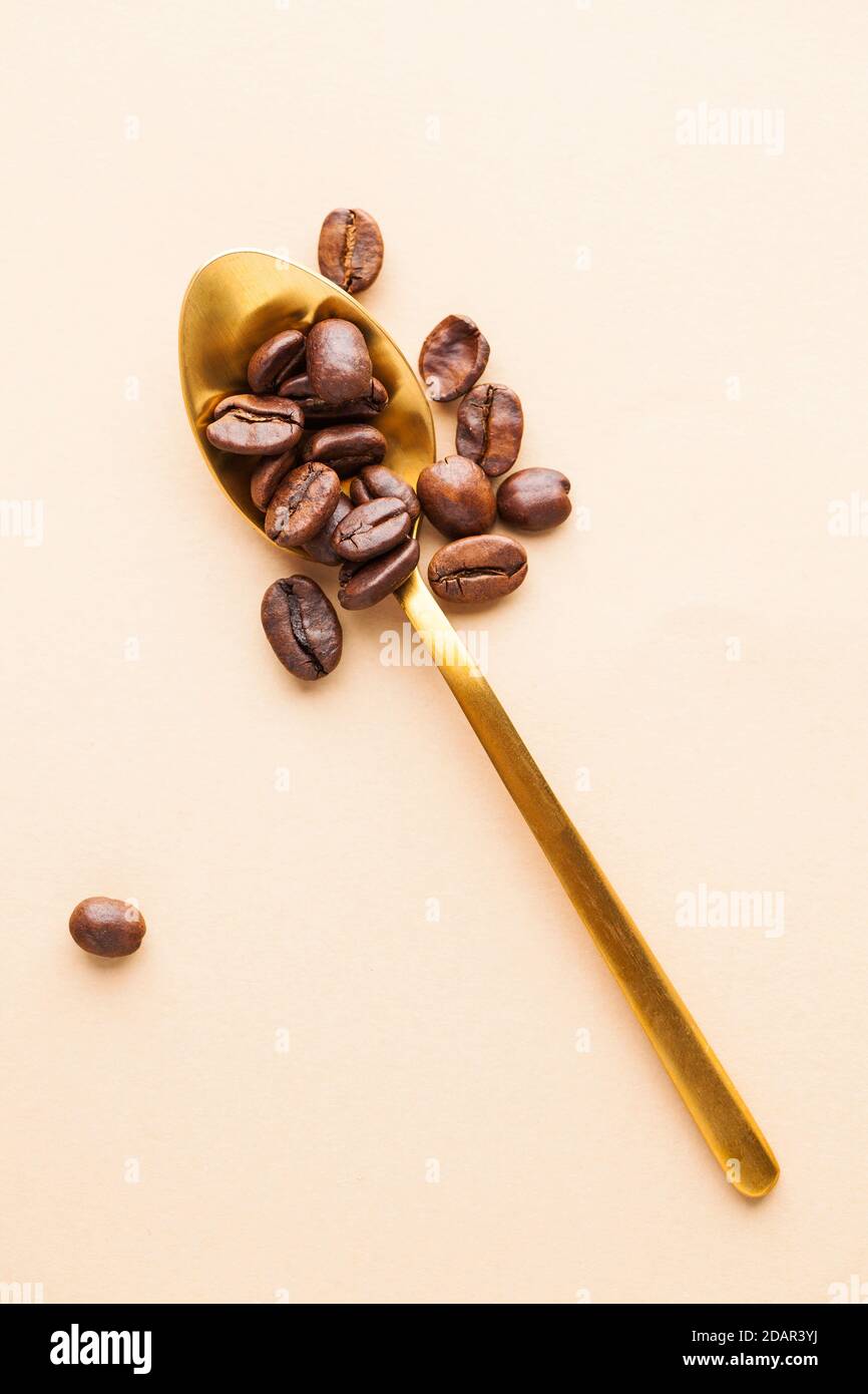 Golden teaspoon with coffee beans arabica beans on a light brown ...