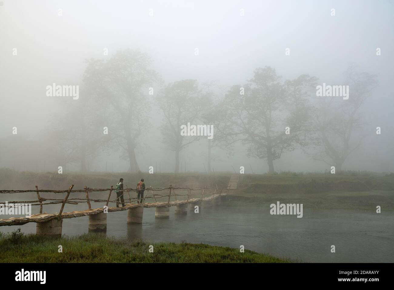 Two men walk in the morning fog over a bridge over the Rapti River ...