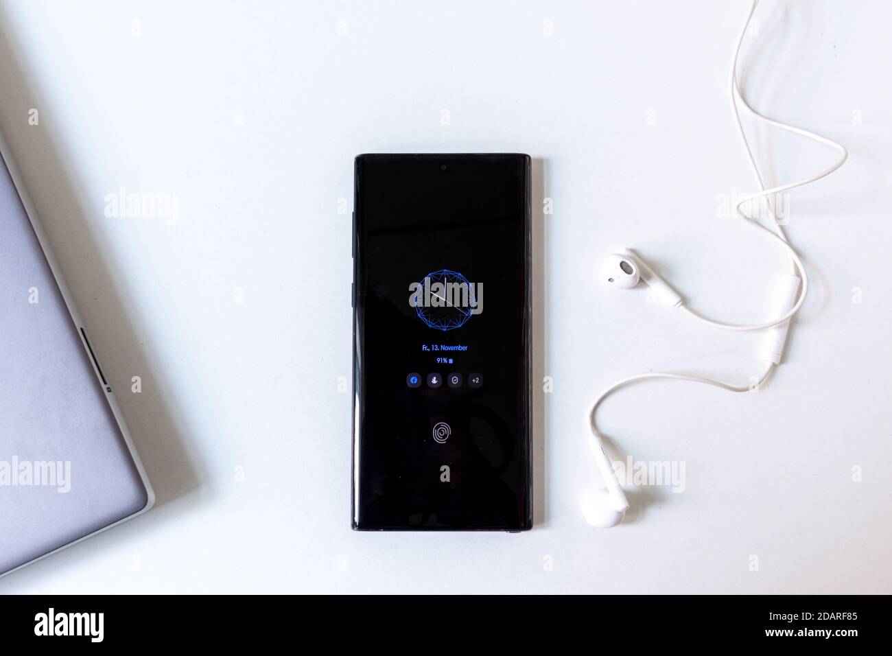 Black smartphone with digital blue clock and white earphones laying on ...