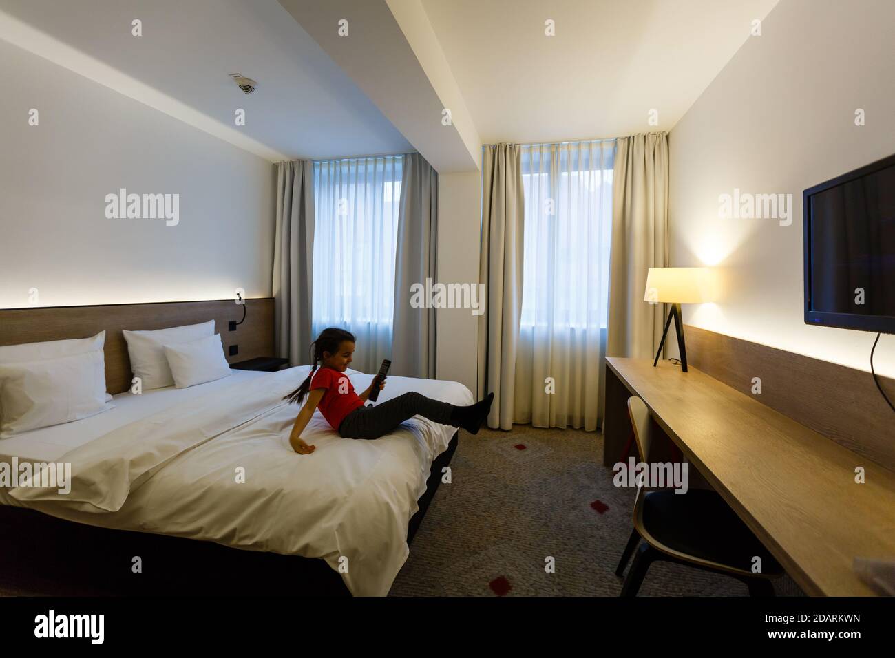 Little girl child with remote control watching tv set lying on bed in ...