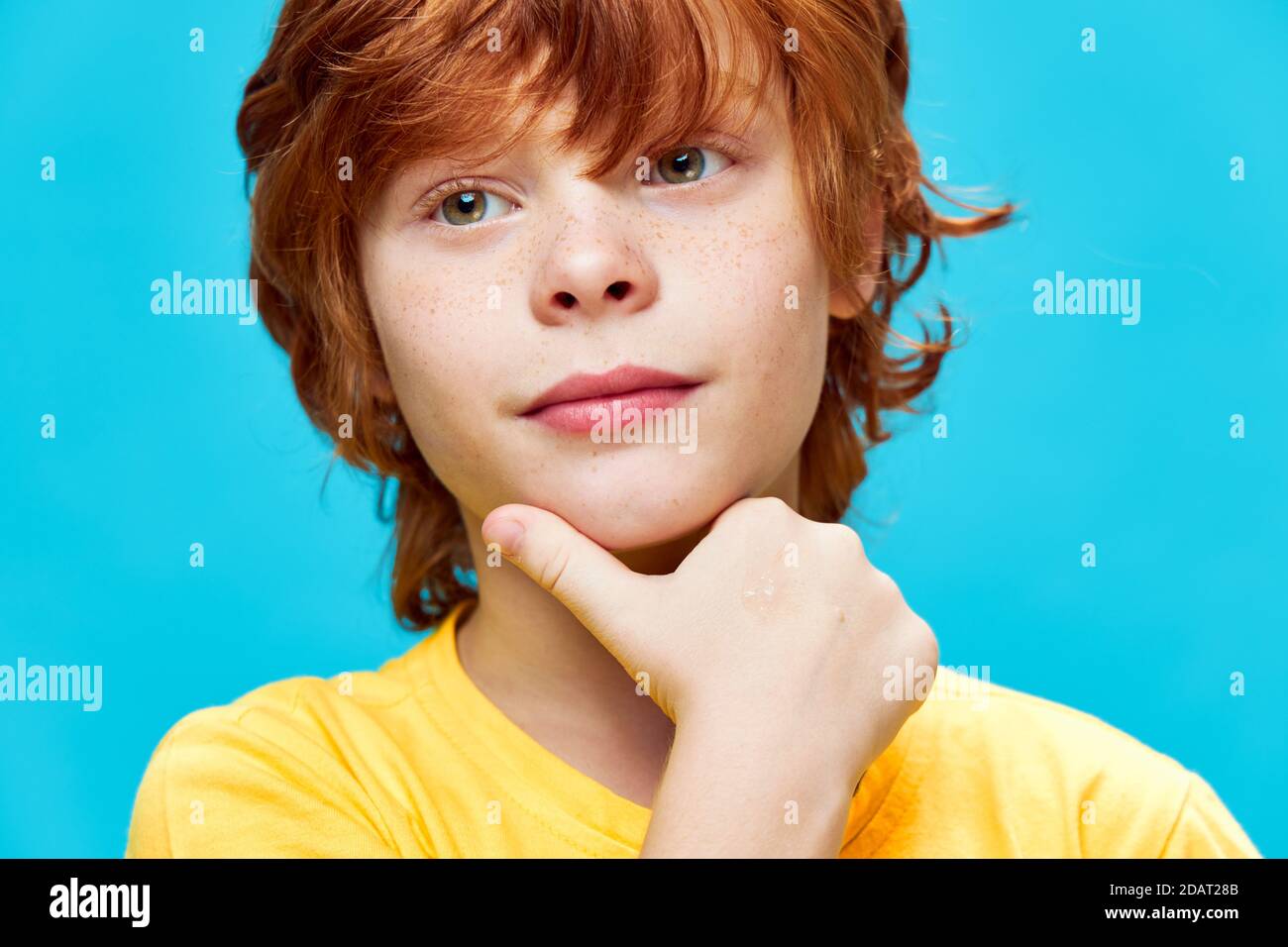 Boy with red hair holds his hand on his chin face close-up cropped view ...