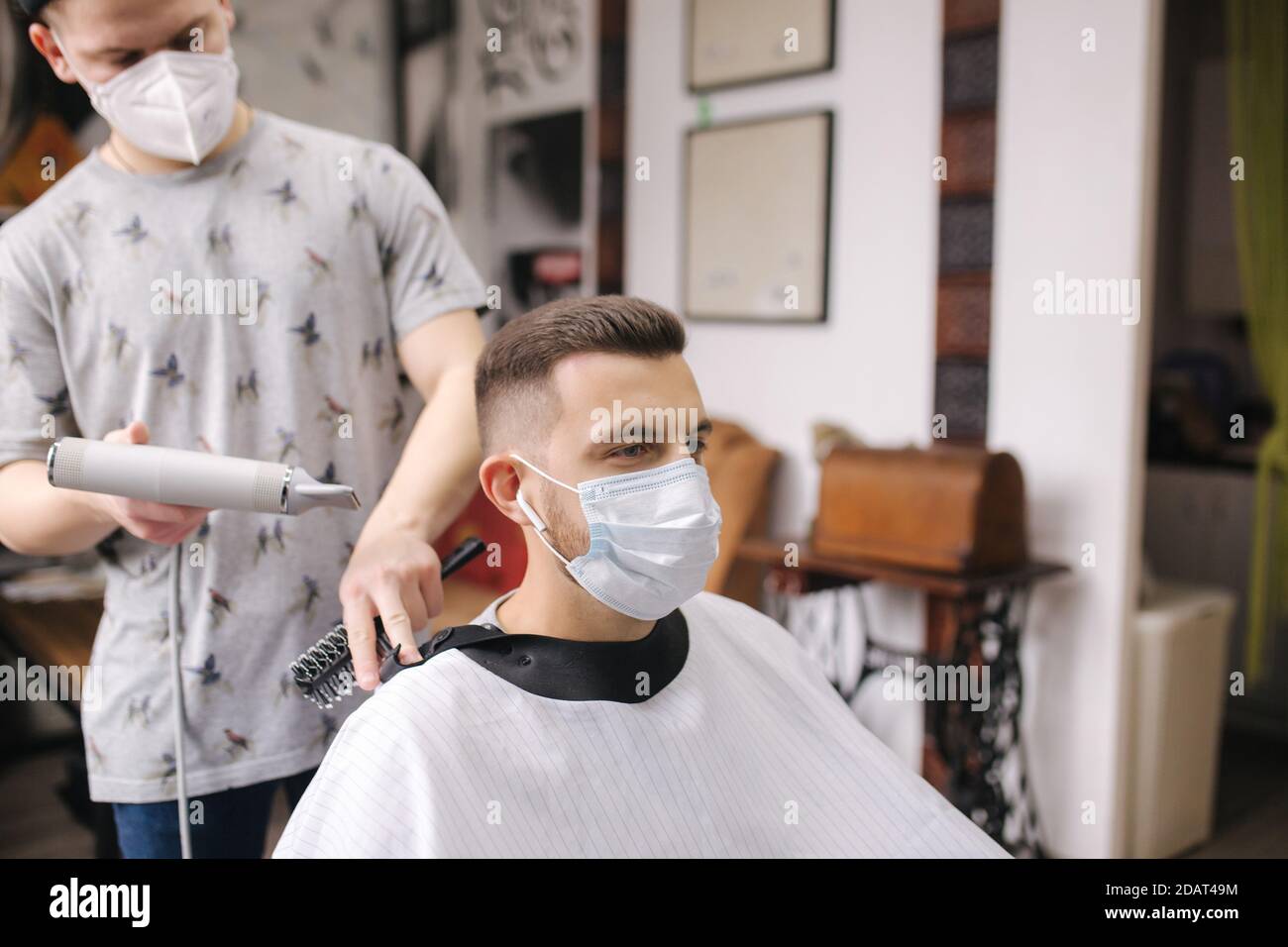 Barber cutting hair to a handsome bearded man in face mask. Protective ...