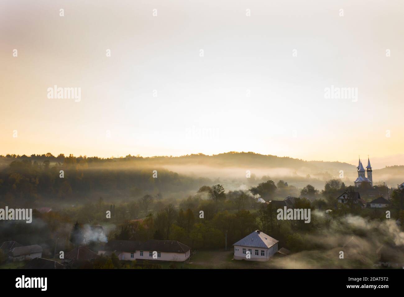 Aerial view of village in fog with golden sunbeams at sunrise in autumn ...