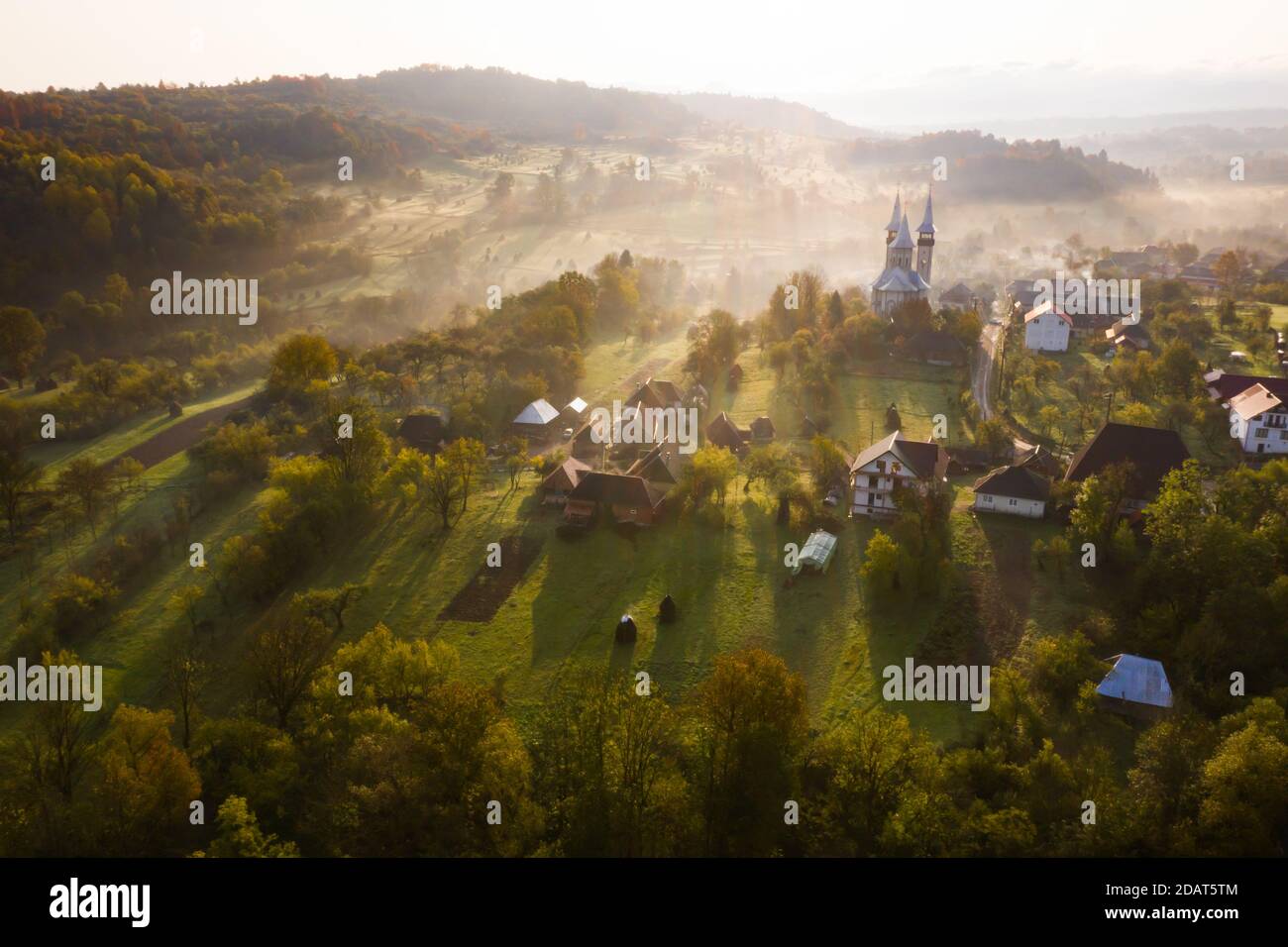 Aerial view of village in fog with golden sunbeams at sunrise in autumn ...