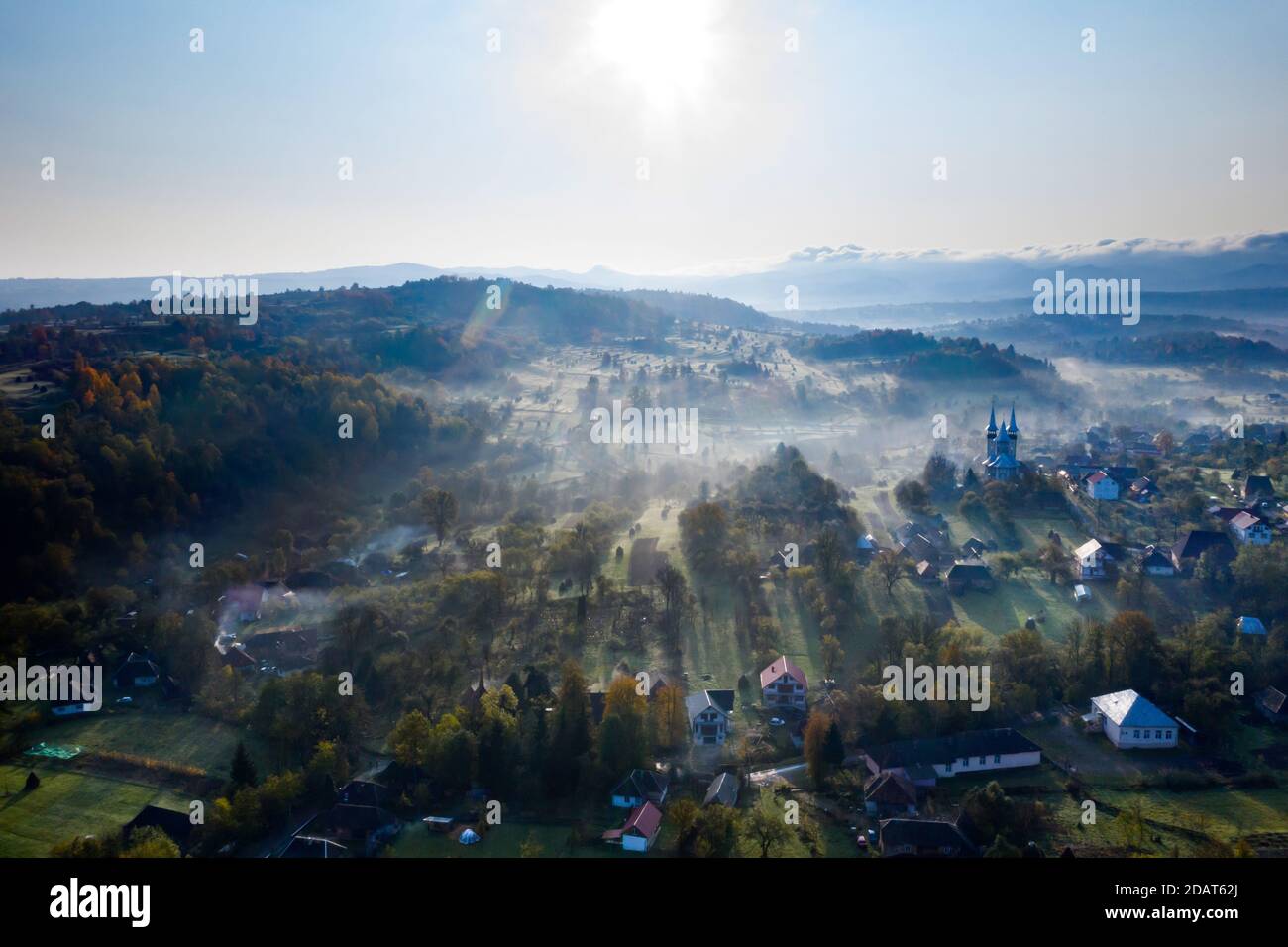 Aerial view of village in fog with golden sunbeams at sunrise in autumn ...