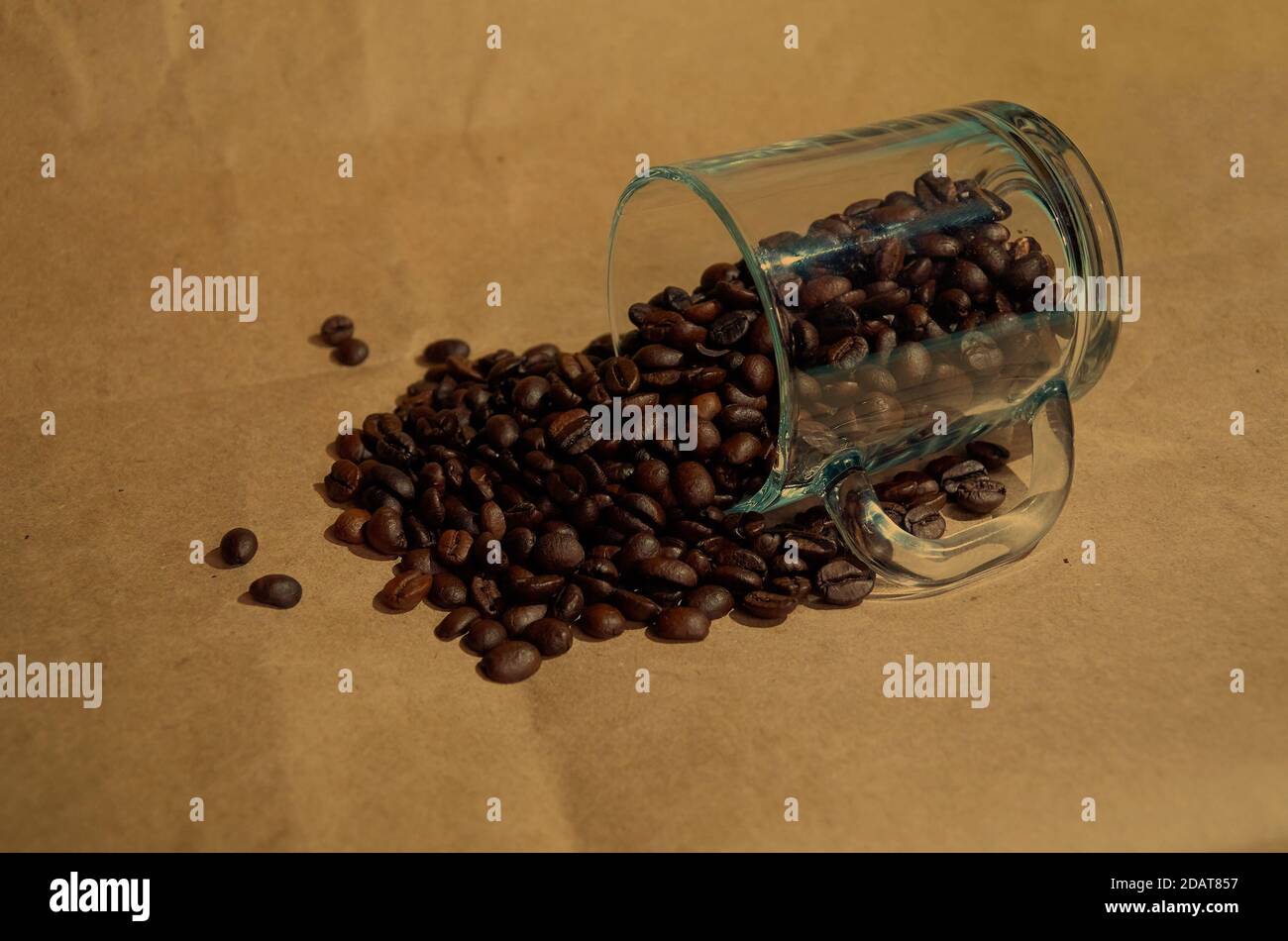 roasted coffee beans spilled out of a clear glass Cup on a brown ...