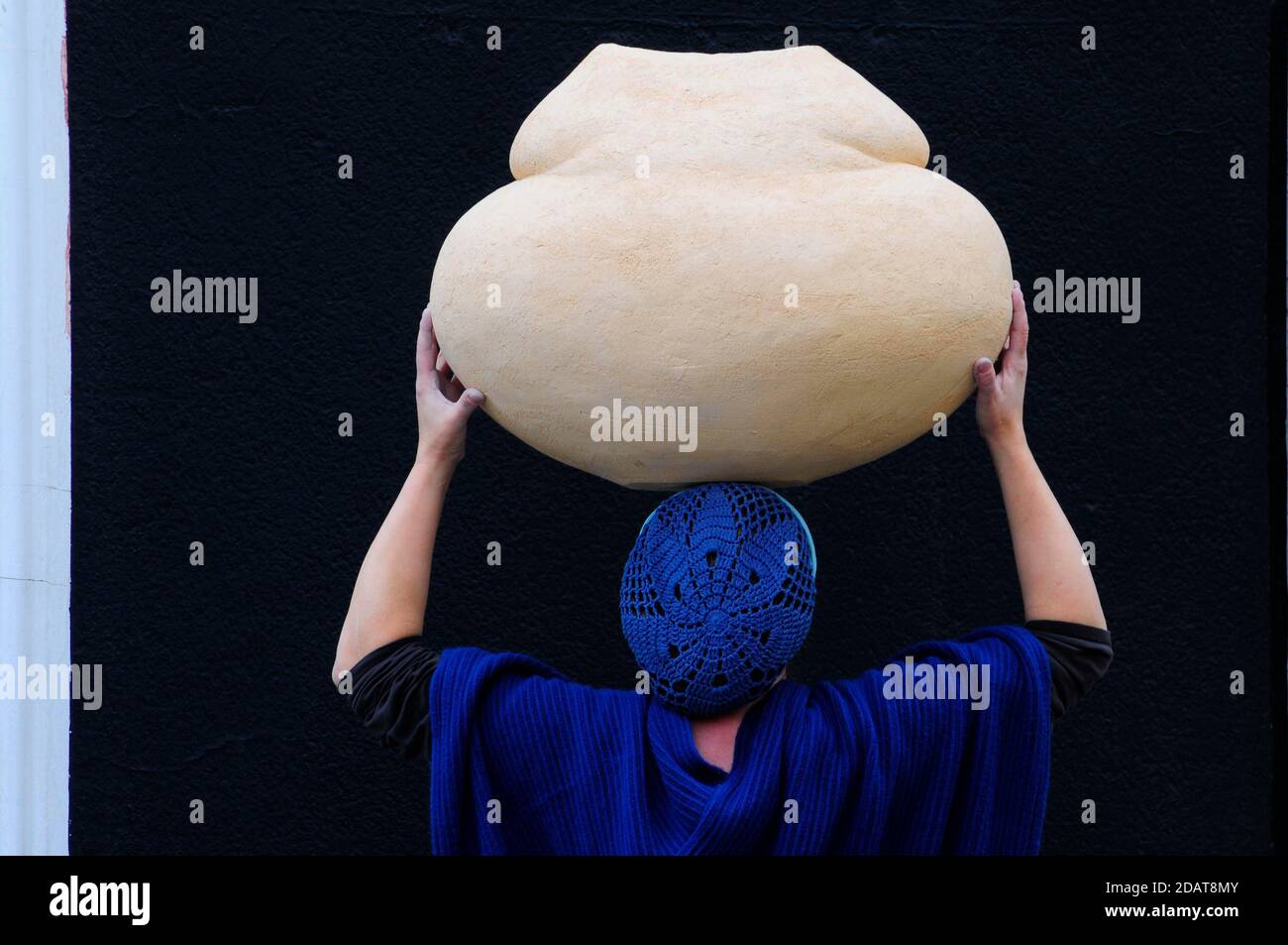 woman in blue clothes transporting a big pottery vessel on her head ...