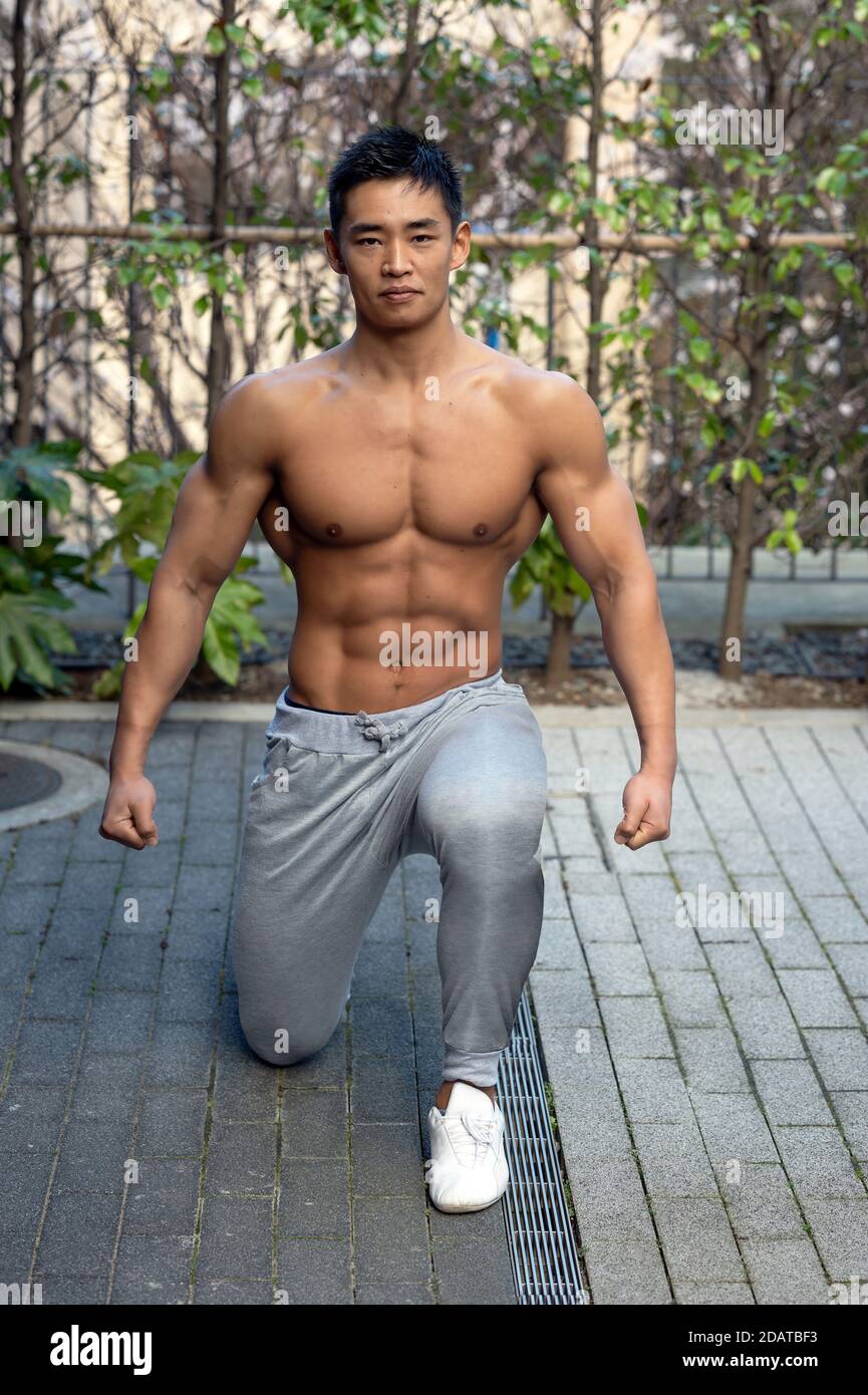 A muscular male Japanese amateur bodybuilder poses outdoors in a street ...