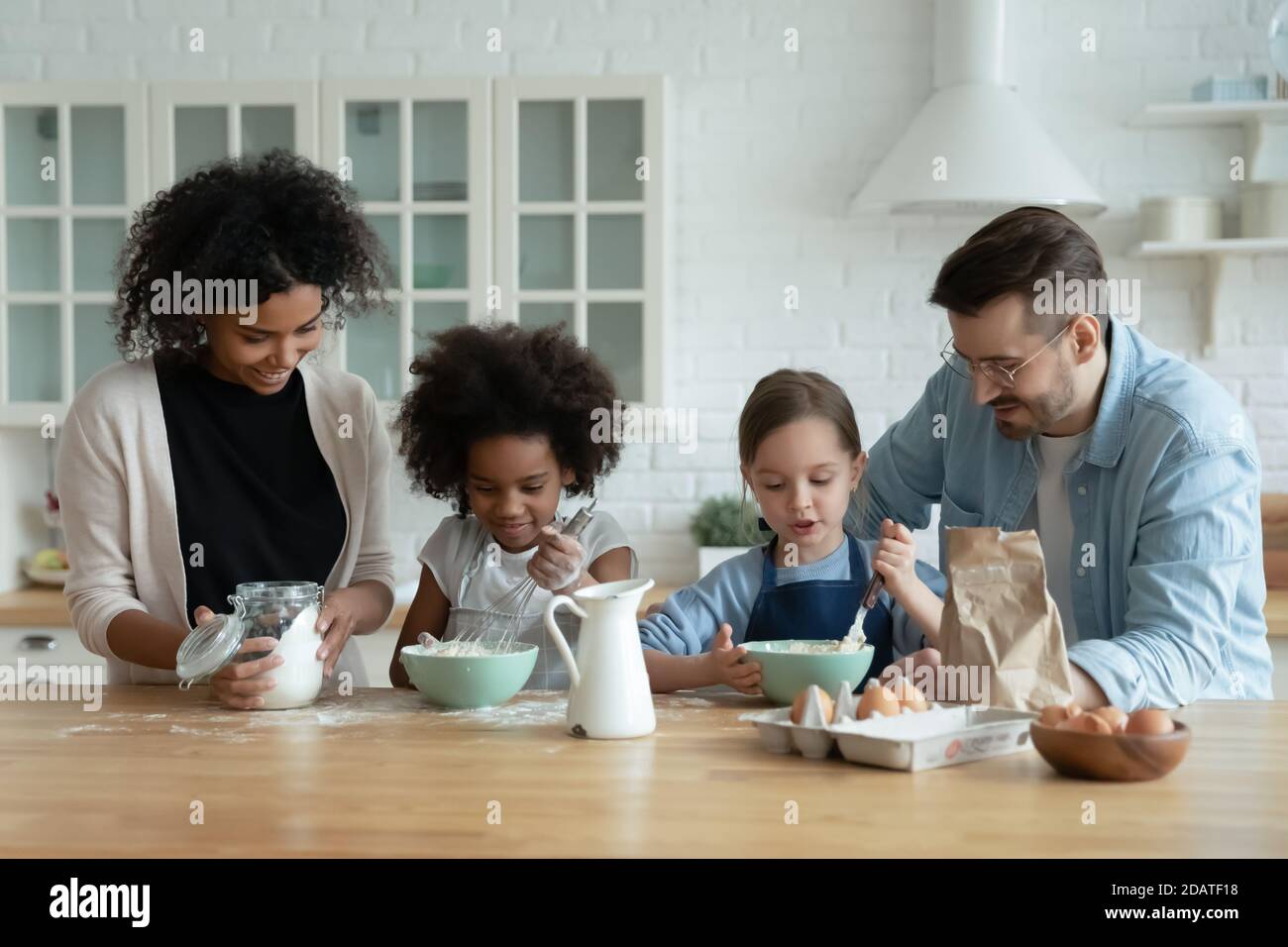 Happy diverse parents with two daughters cooking pancakes in kitchen ...