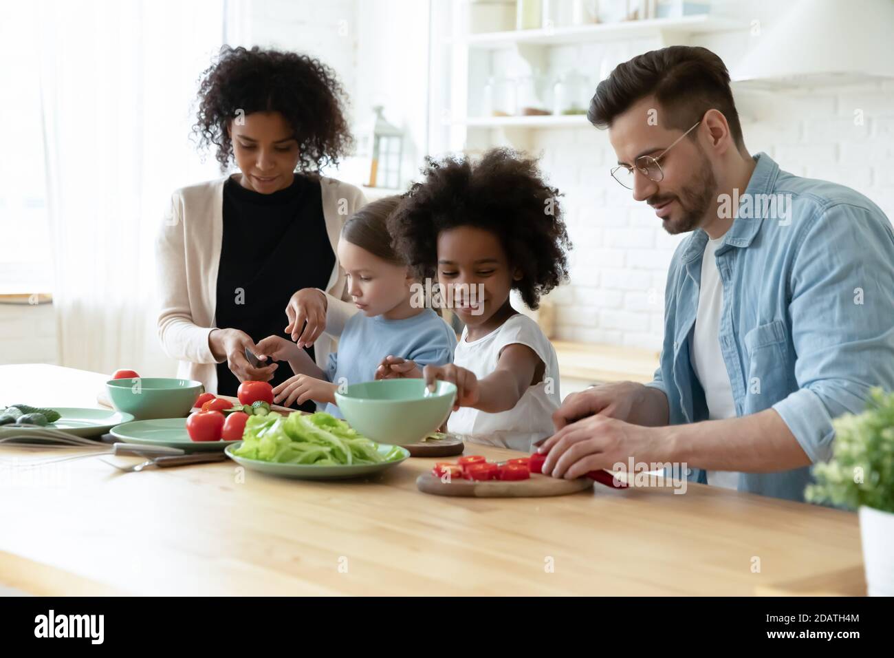 Happy diverse parents with adorable daughters preparing meal together ...