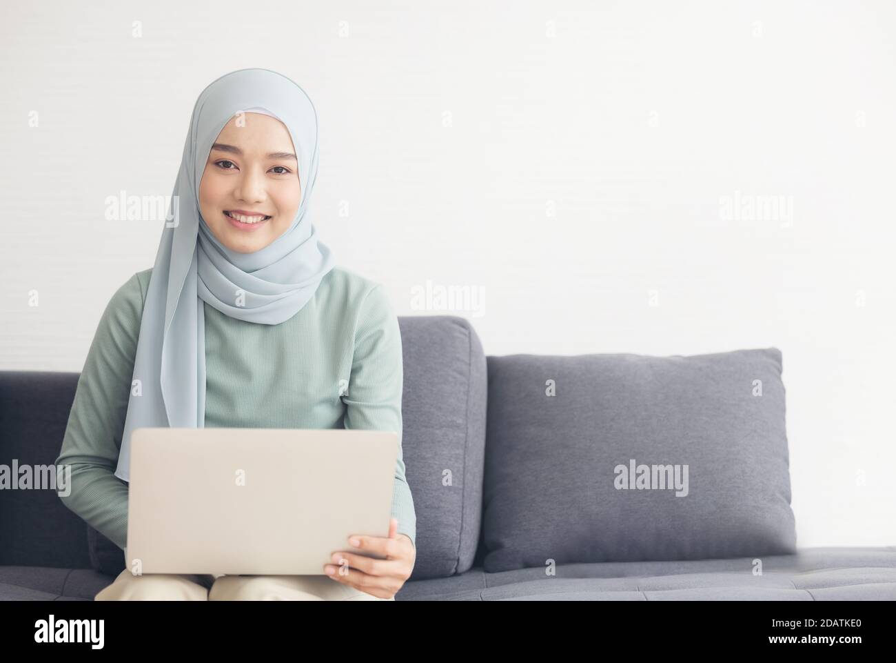Portrait of a young happy muslim woman in hijab working at home using ...