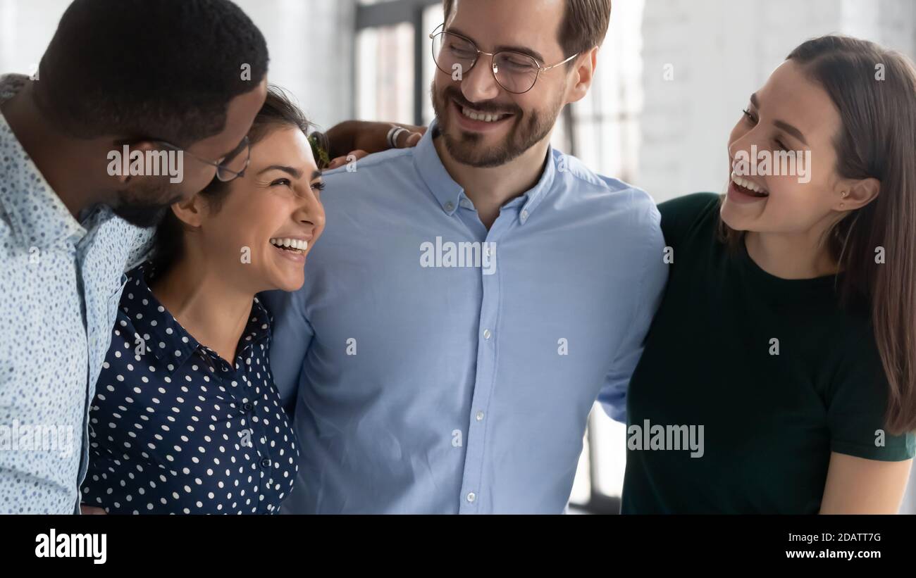 Happy multiethnic teammates hugging in office corridor demonstrating ...