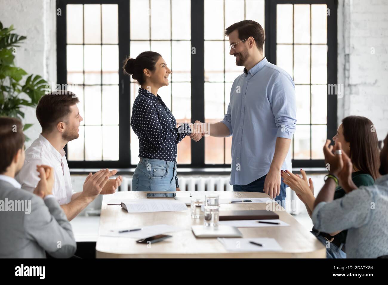 Young caucasian male ceo handshaking with indian female team member ...