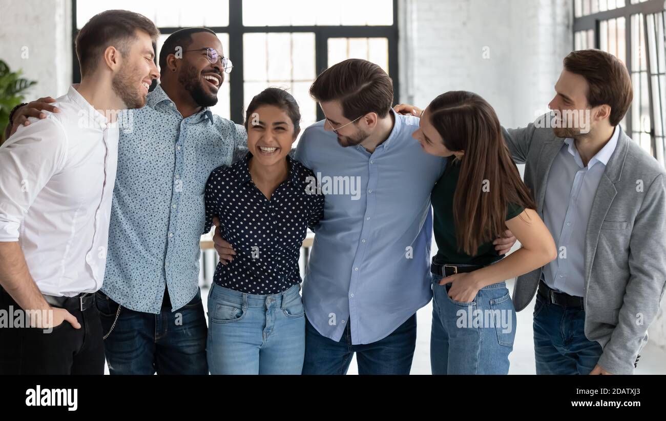 Excited overjoyed millennial multiethnic teammates hugging celebrating ...