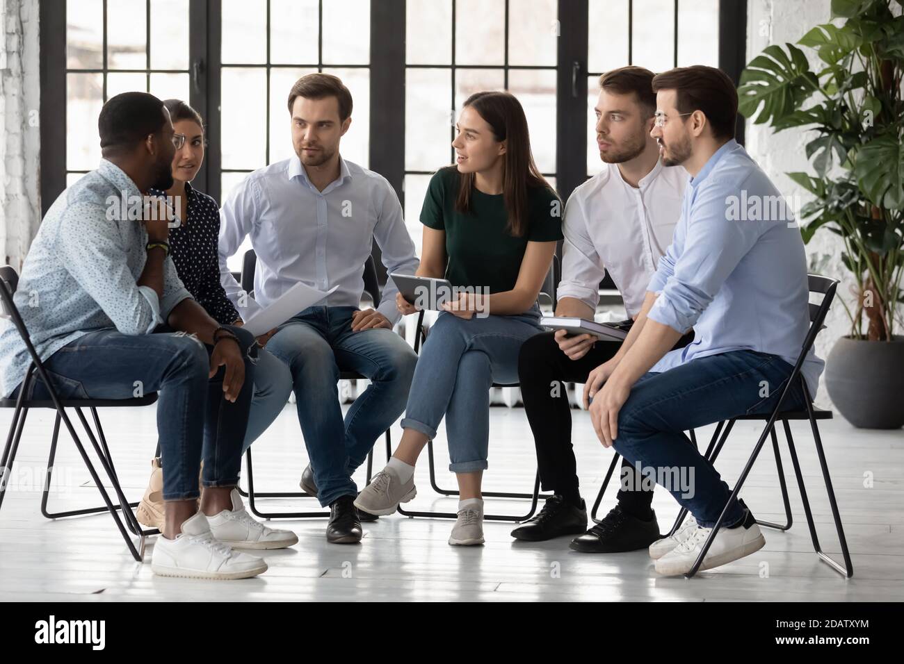 Concentrated diverse teammates sitting on chairs close together ...