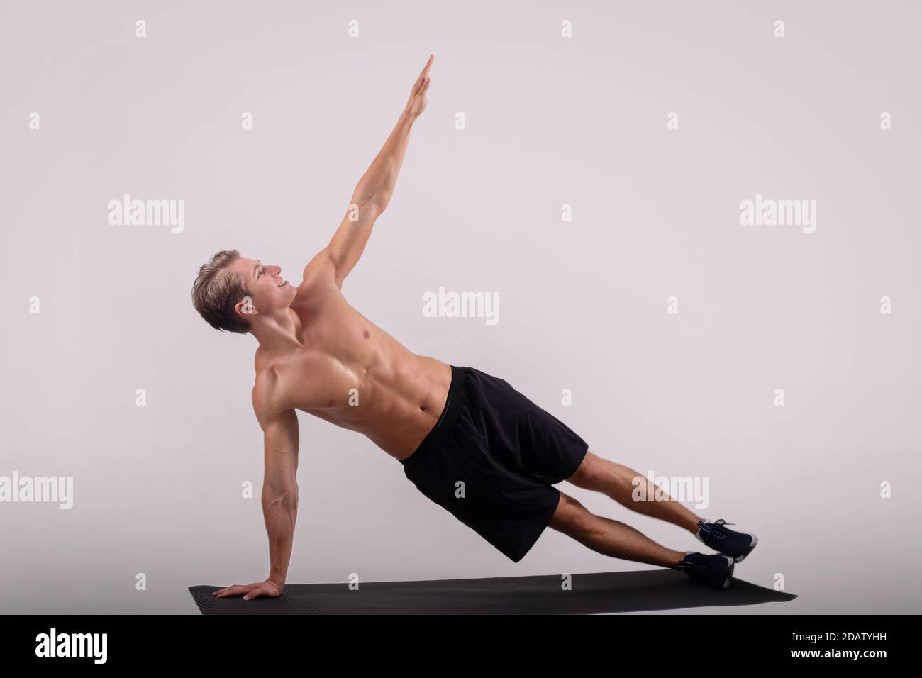 Full length portrait of athletic young guy doing side plank over light ...