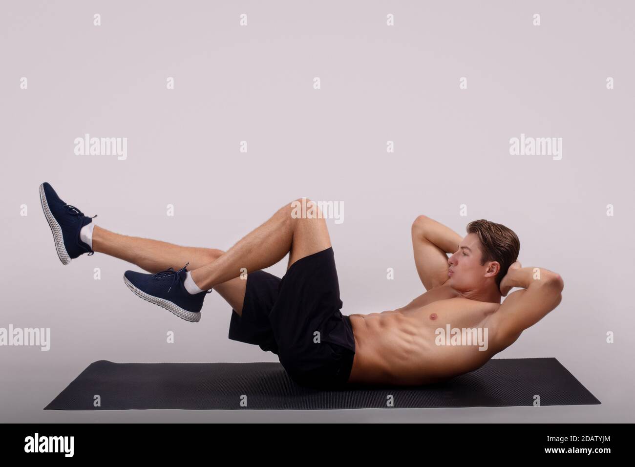 Strong young guy with bare torso doing abs exercises on yoga mat ...