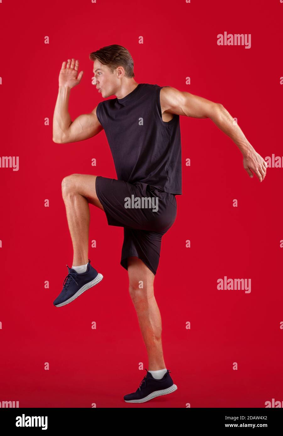 Side view of young male sprinter running, exercising on red studio ...