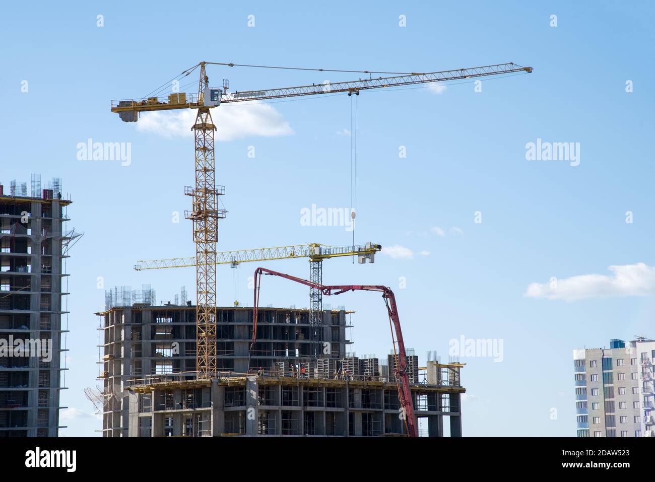 Tower crane lifting a concrete bucket at construction site. Workers ...