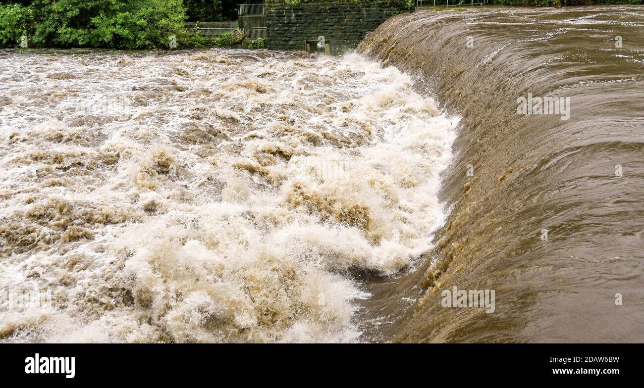 Muddy brown water in a river in flood after a storm flowing fast over a ...