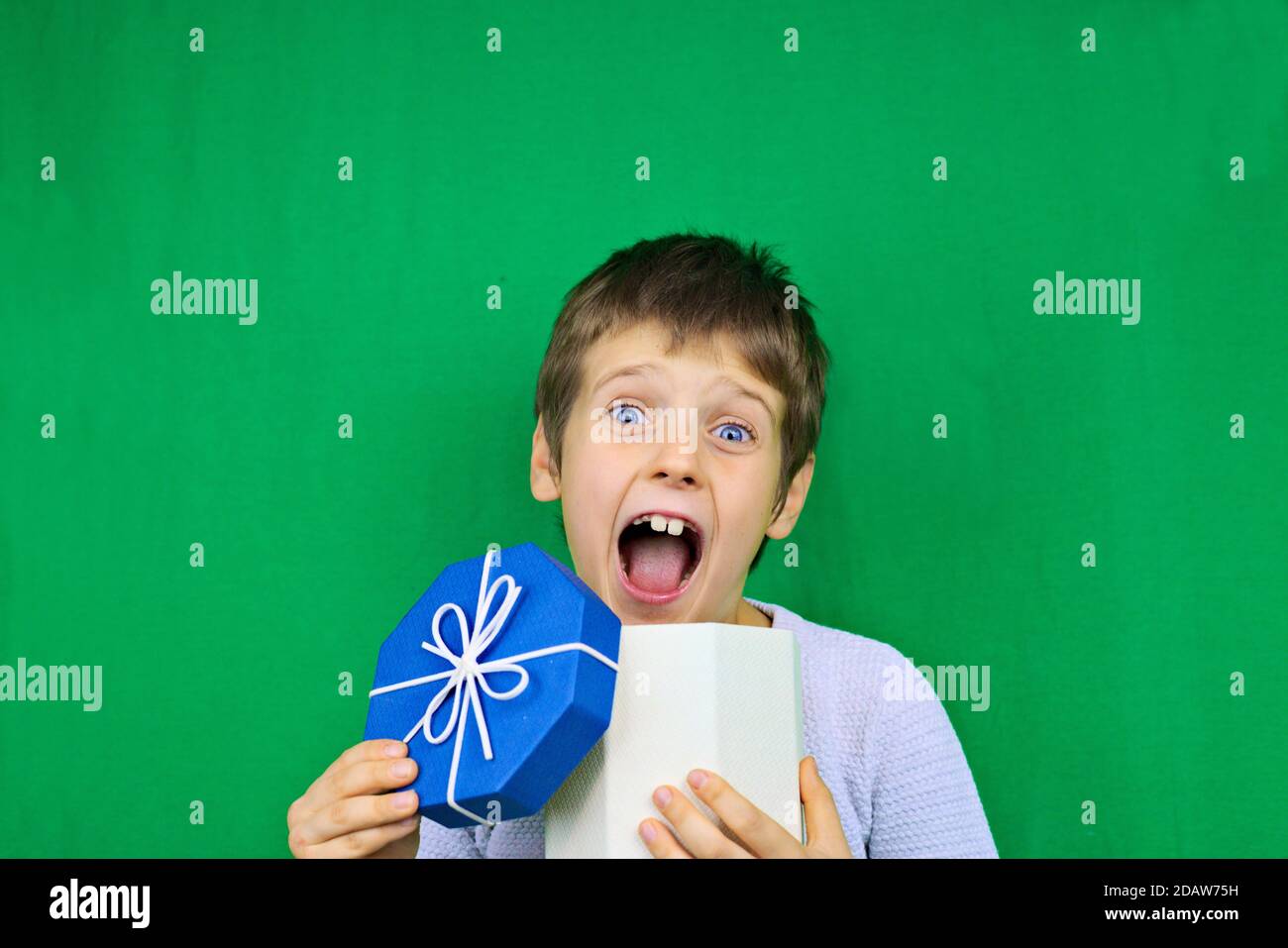 Surprised Caucasian boy holding a gift box and screaming on a green ...