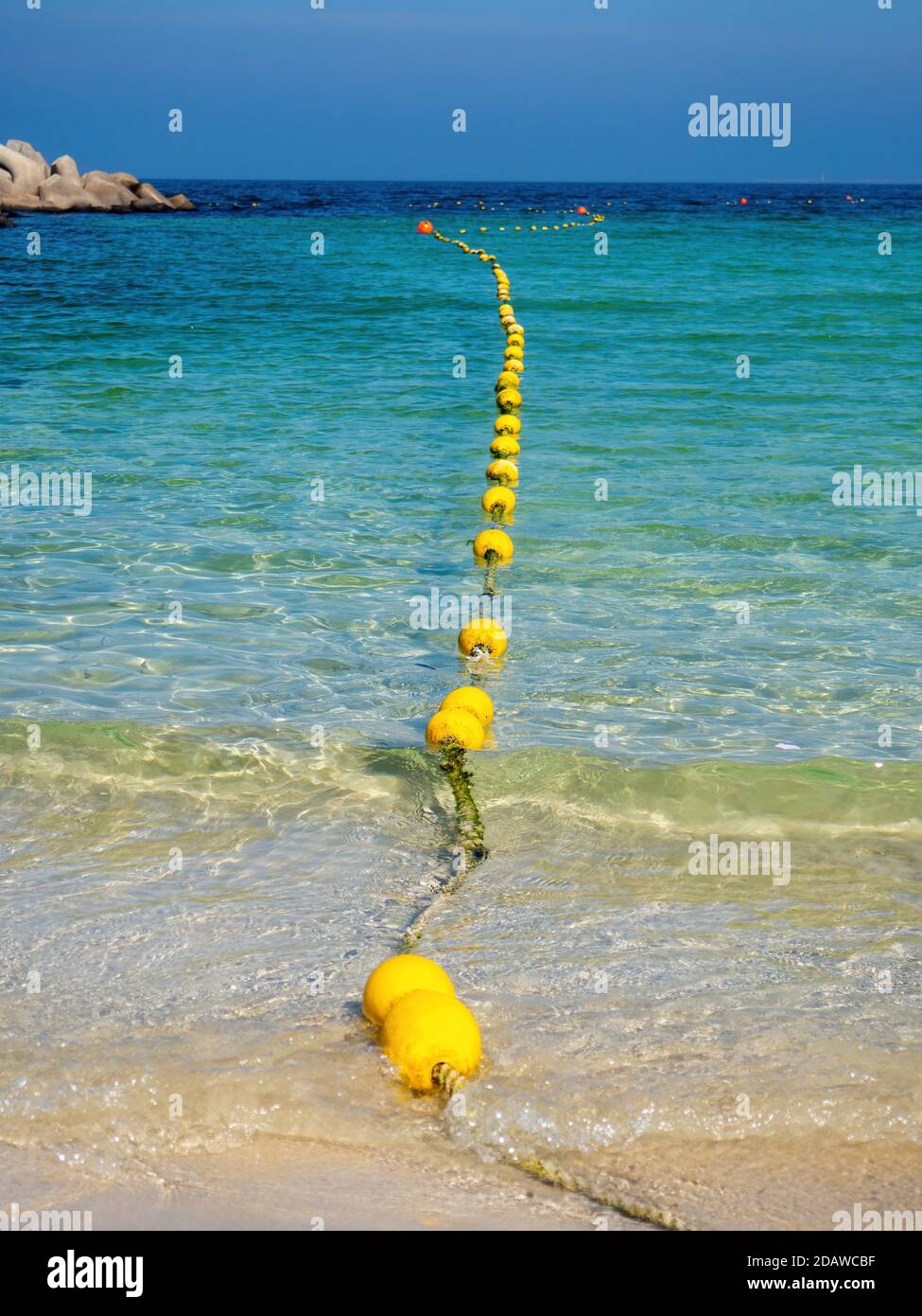 Vertical seascape with floating buoys and rope dividing area on beach ...