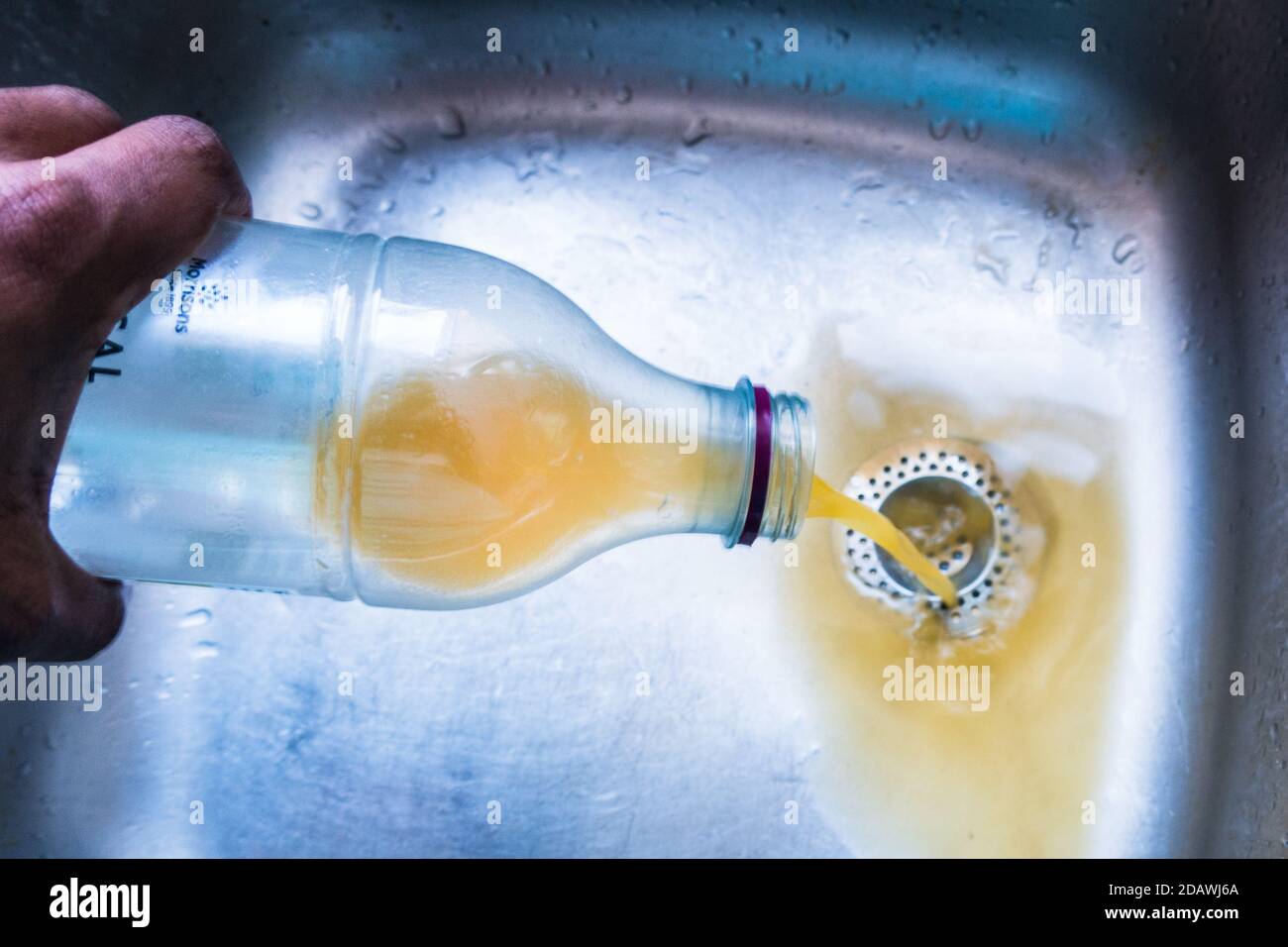 Adult man dumping fruit juice from plastic bottle into kitchen drain ...