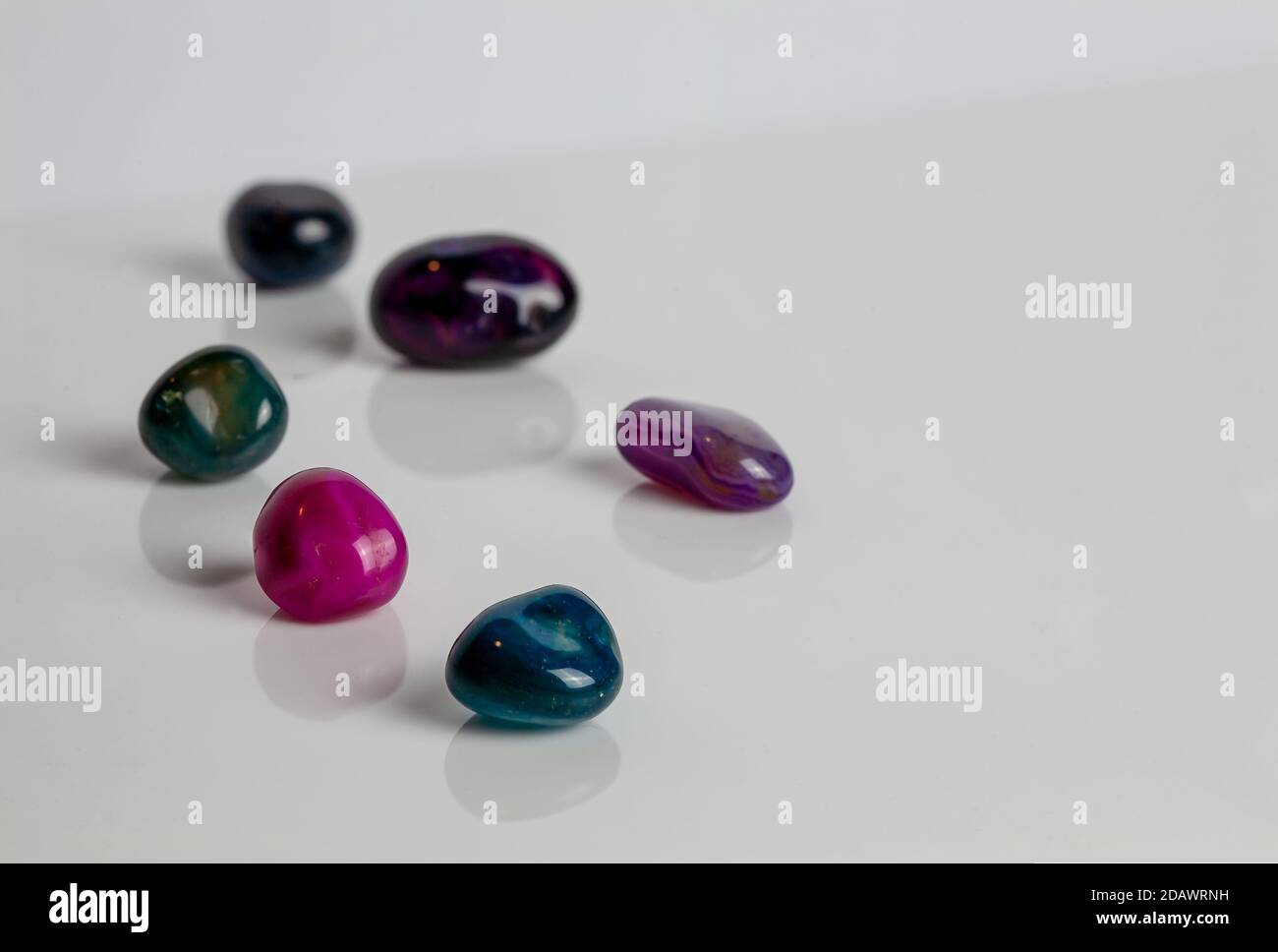 Colored gemstones scattered on a plain white reflective background ...
