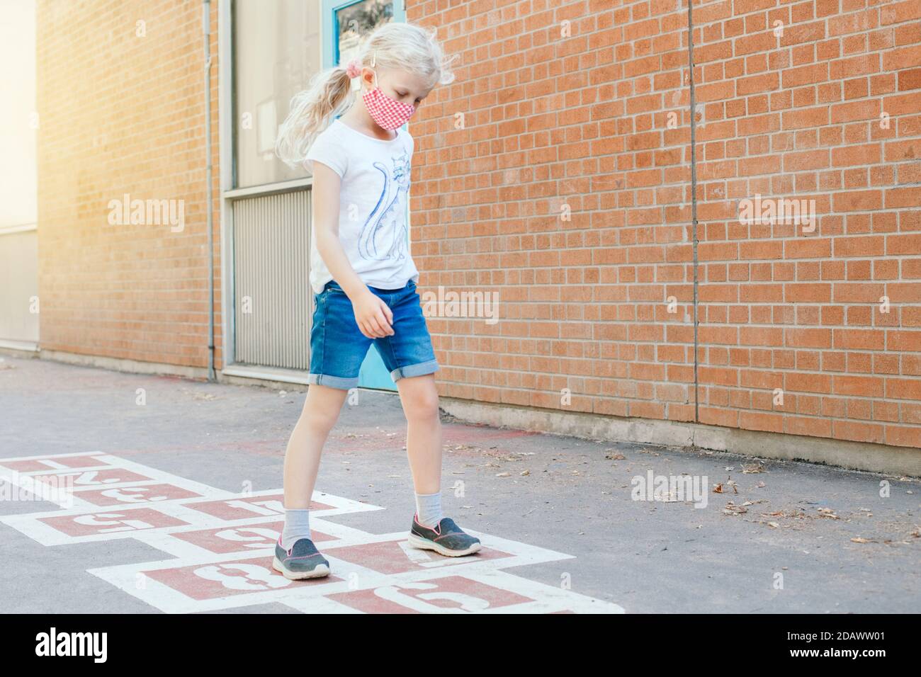 Child girl in face mask playing jumping hopscotch on school yard. Funny ...