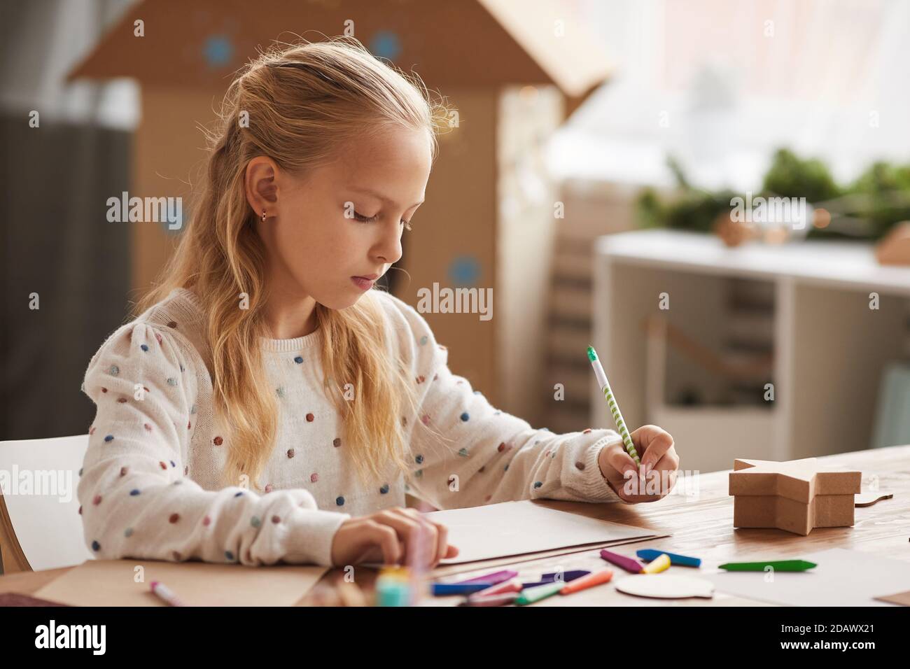 Portrait of blonde teenage girl drawing or doing homework while sitting ...