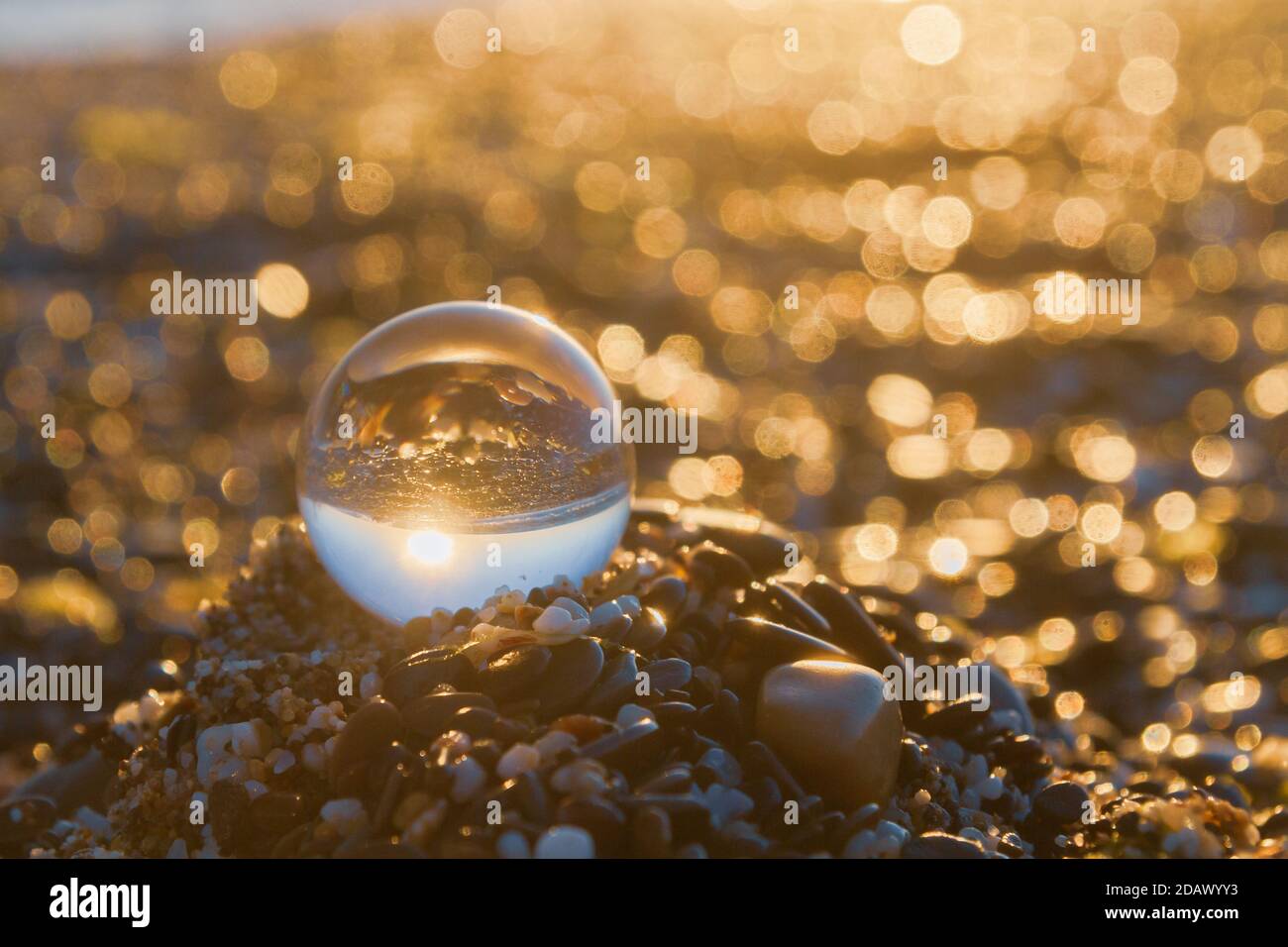 Glass round ball on the beach reflects the sea in summer at sunset ...