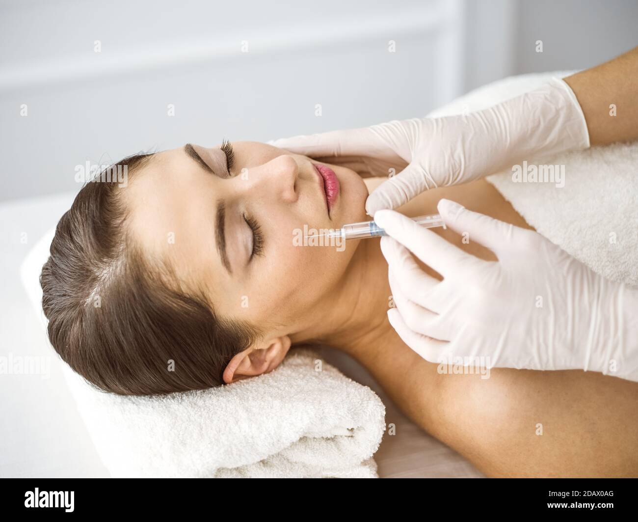 Beautician doing beauty procedure with syringe to face of young brunette woman in clinic ...