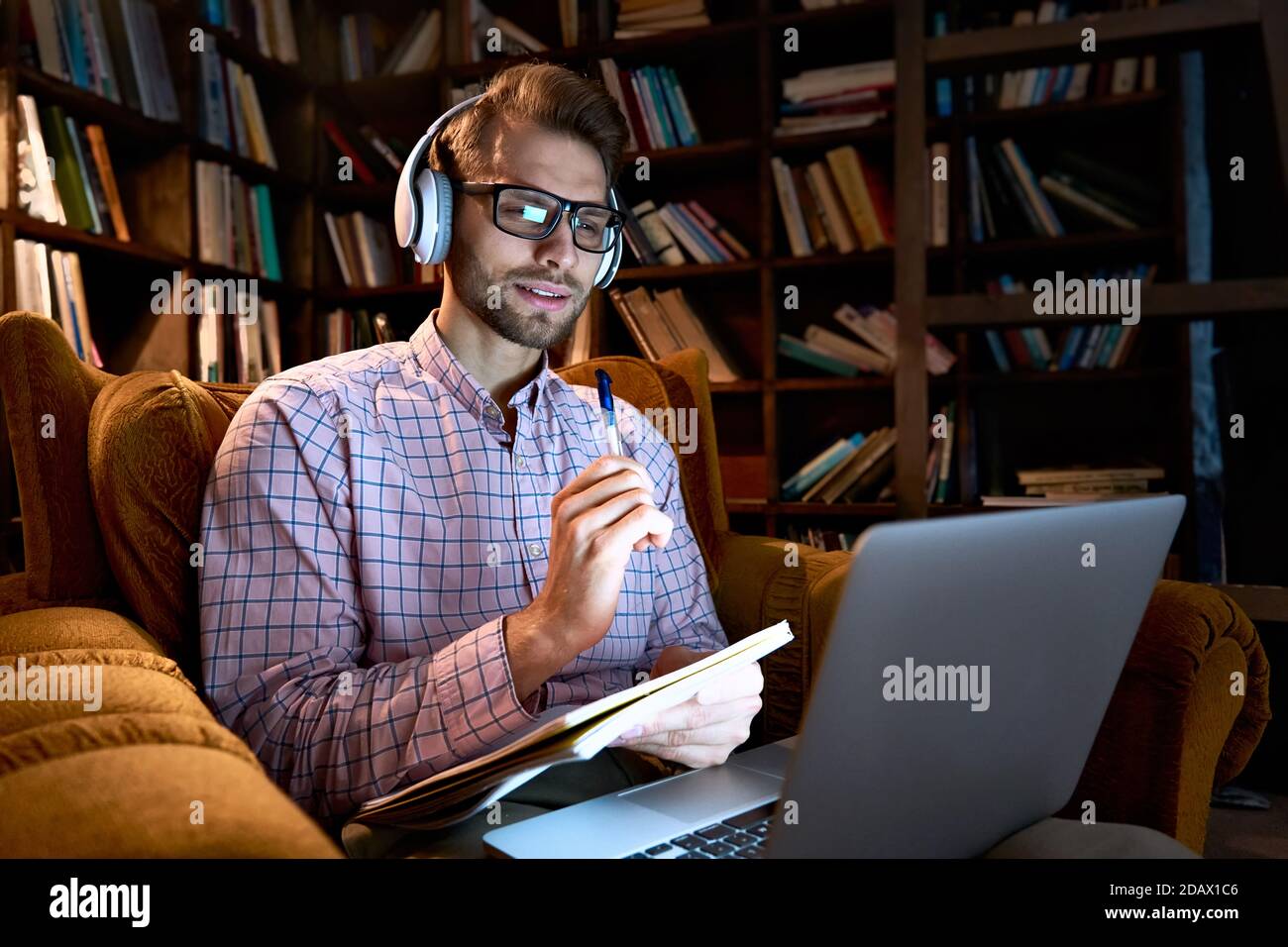 Male student wearing headphones elearning on laptop online, watching ...