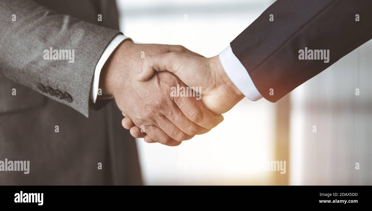Business people standing and shaking hands in sunny office, close-up ...