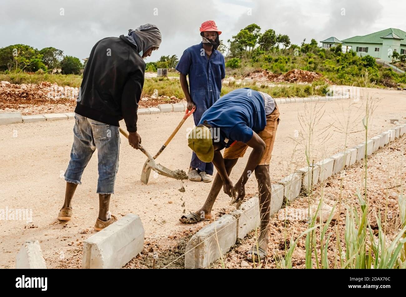 Three men at work on a road construction site. While one bend over to ...