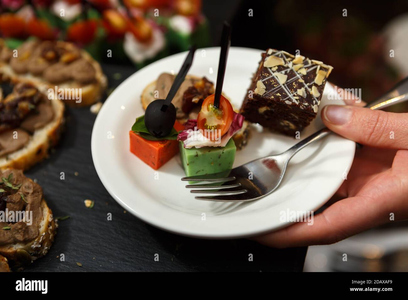 Hand holding a plate of canapes and cakes closeup Stock Photo - Alamy