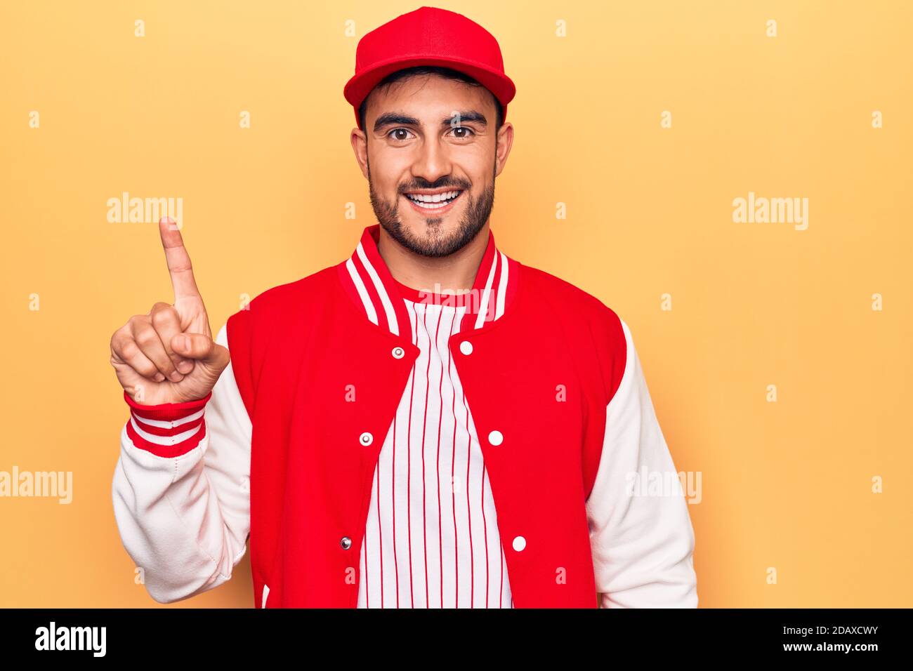 Handsome sporty man with beard wearing baseball jacket and cap over ...
