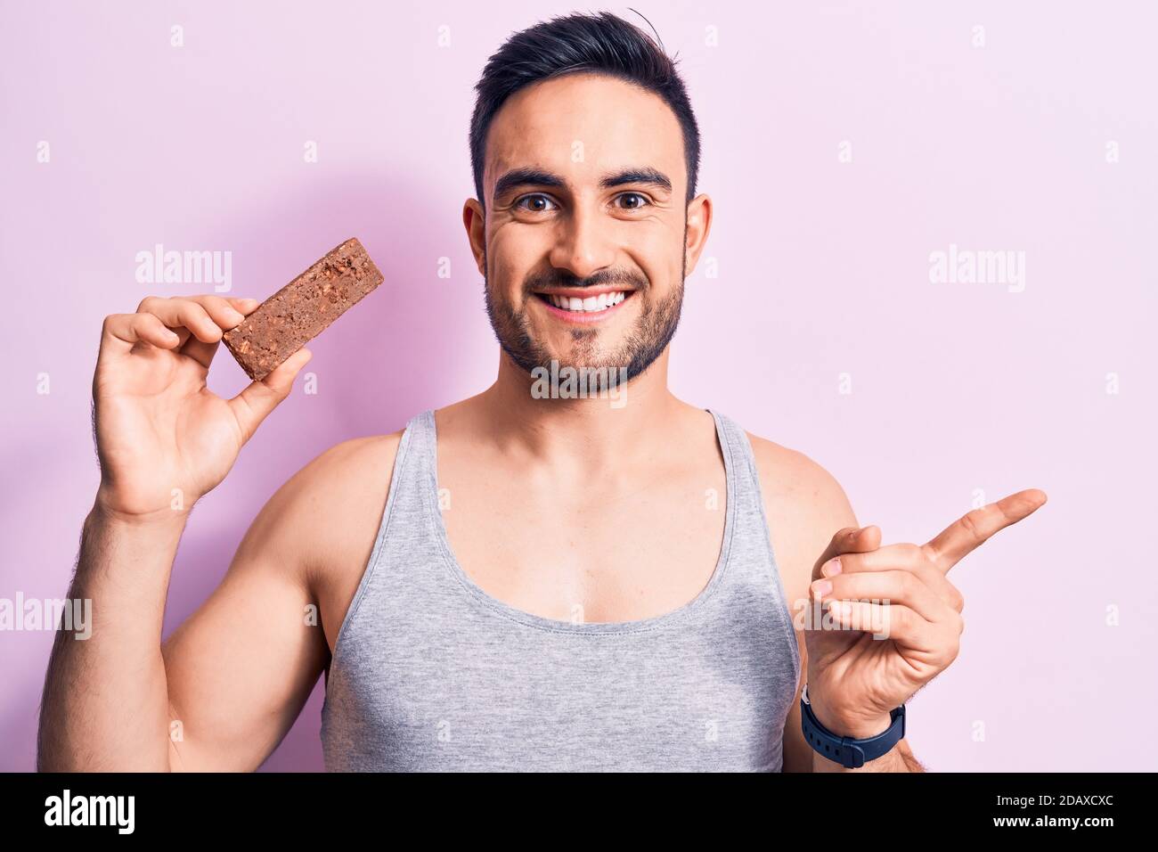Young handsome man with beard eating energy protein bar over isolated ...
