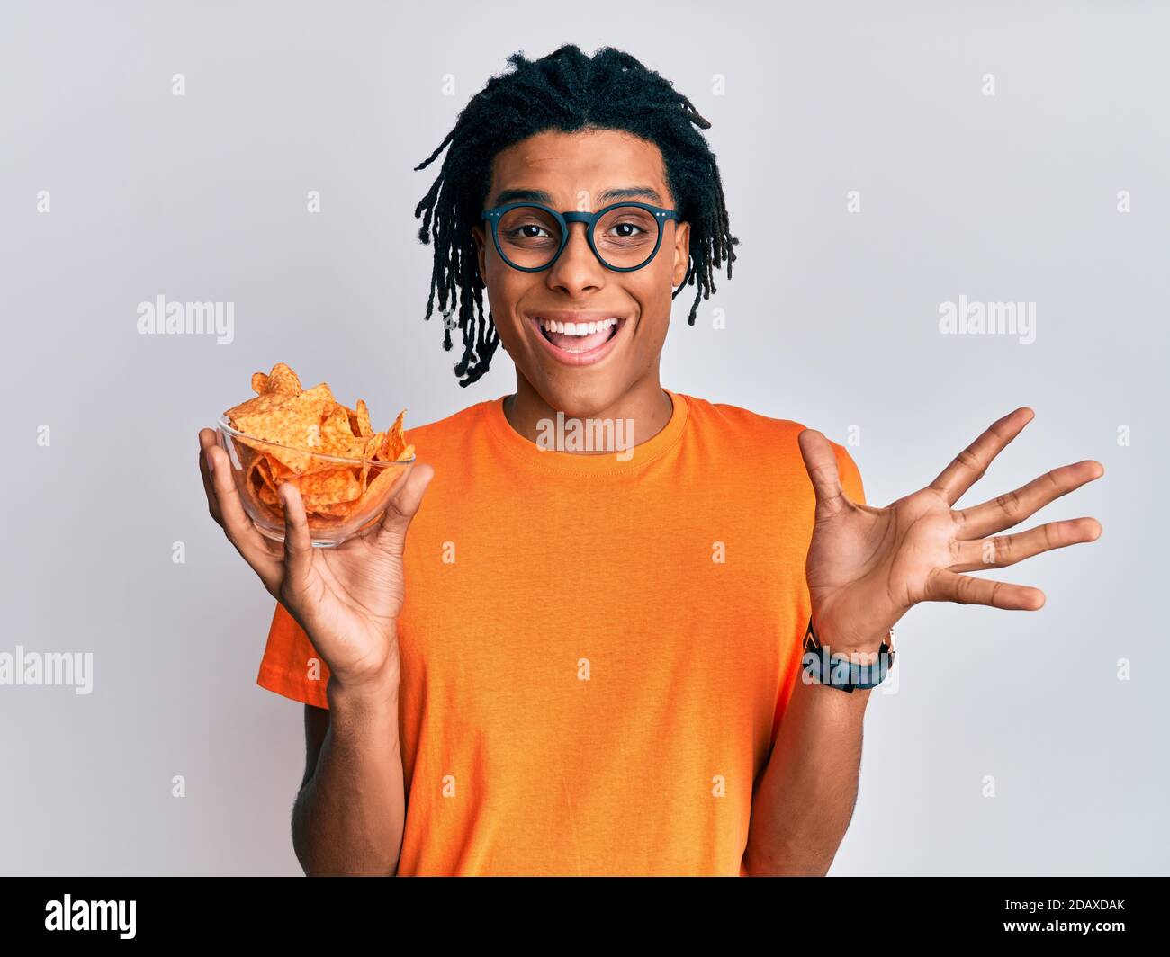 Young african american man holding nachos potato chips celebrating ...